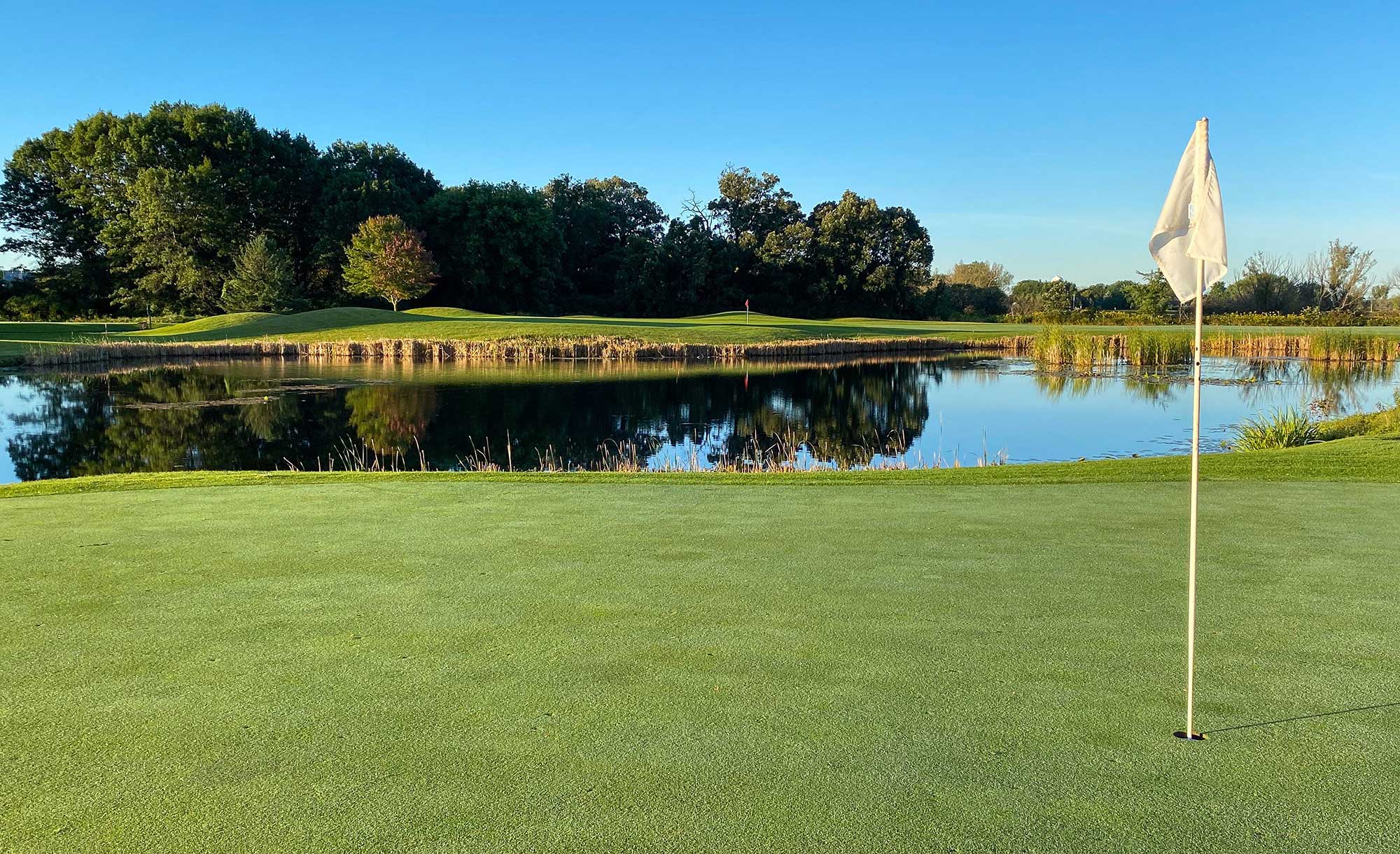 A white flag on a green golf course with a pond.